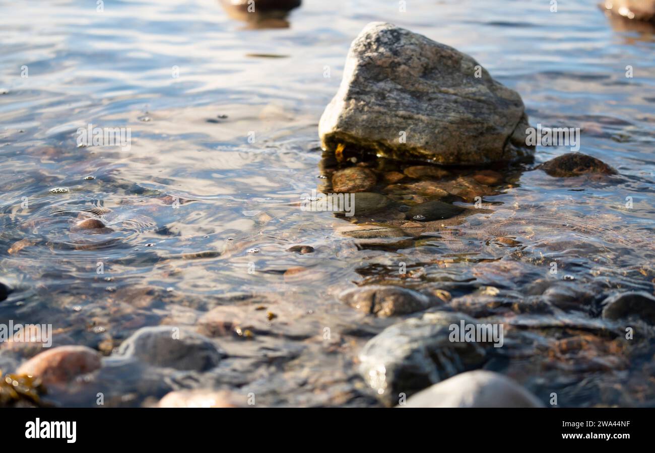 Round stones in the shore water on a calm and clear day in the ...