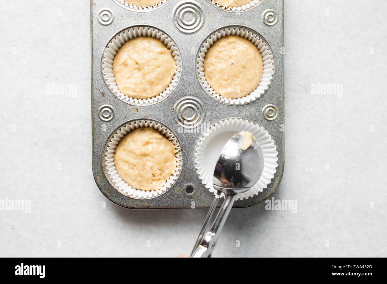 scooping vanilla almond muffins batter in a cupcake pan, top view of ...