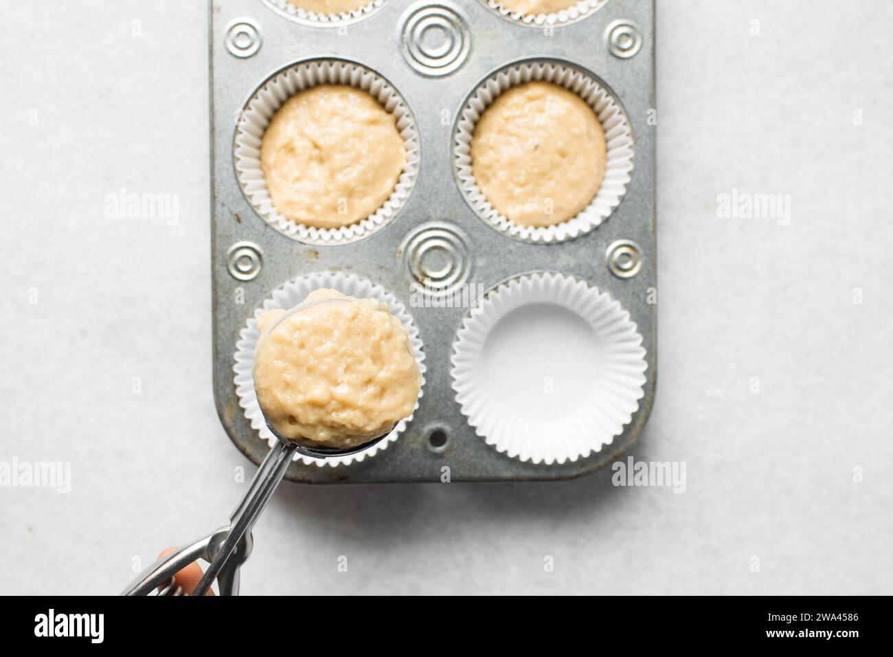 scooping vanilla almond muffins batter in a cupcake pan, top view of ...