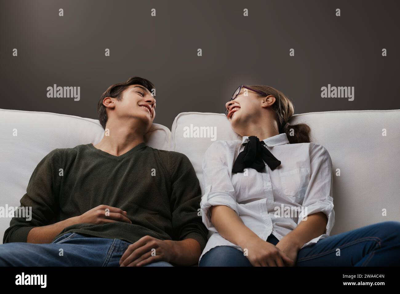 Shared laughter between a young man and woman lounging on a sofa captures a moment of genuine ...