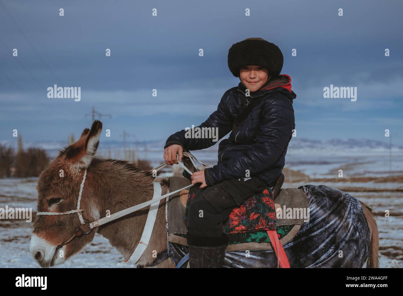 TAU SAMALY, KAZAKHSTAN - DECEMBER 23, 2023: Kazakh boy riding a donkey ...