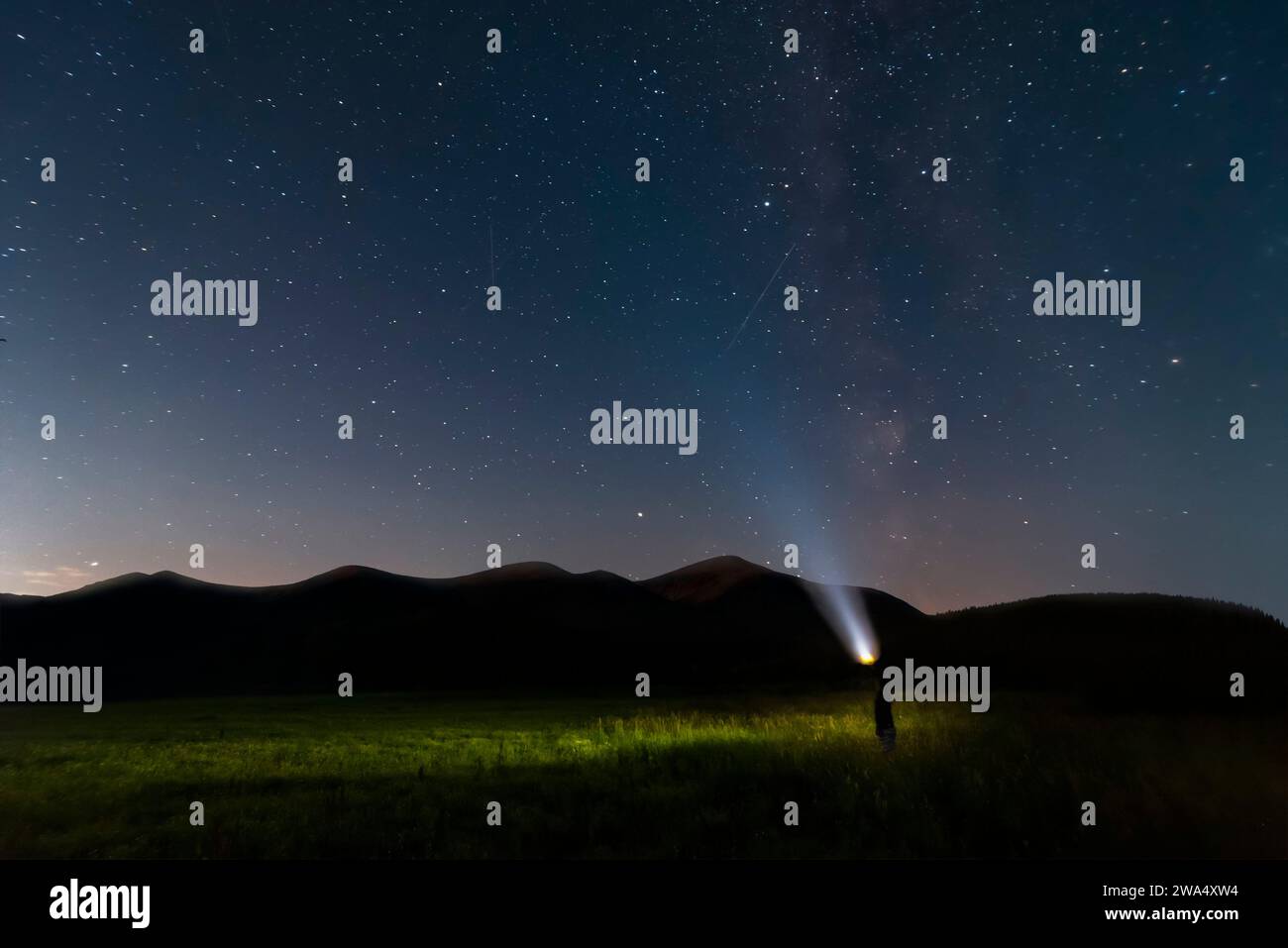 Starry night sky over mountains and man with a flashlight. Natural ...