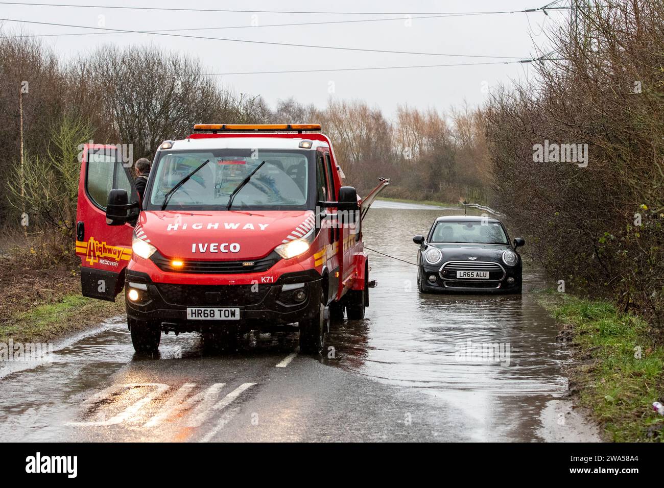 A highway recovery van pulls a car stuck on the flooded road caused by ...