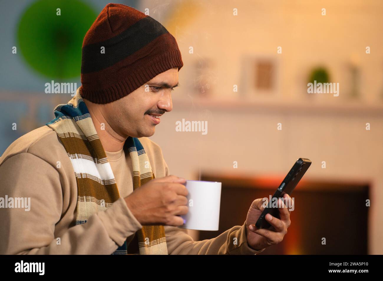 Middle Aged Indian Man With Warmth Winter Wear Using Mobile Phone By Drinking Tea At Home 9119