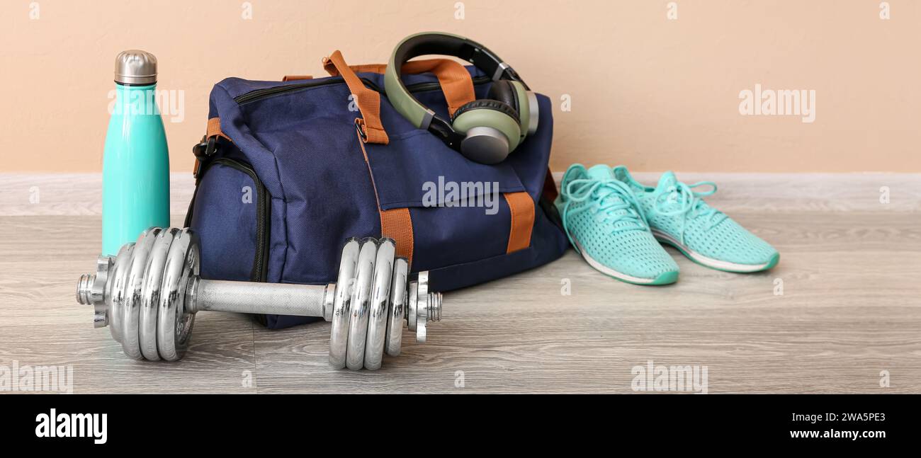 Sports bag with headphones, shoes , dumbbell and bottle near beige wall ...