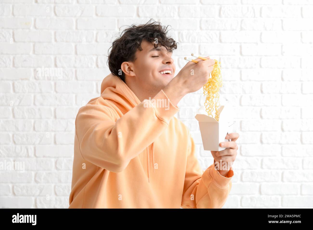 Young man eating tasty Chinese food on white brick background Stock ...