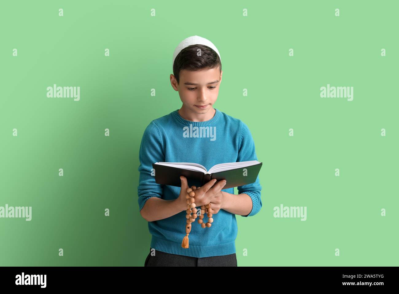 Little Muslim boy with Quran and praying beads on green background ...