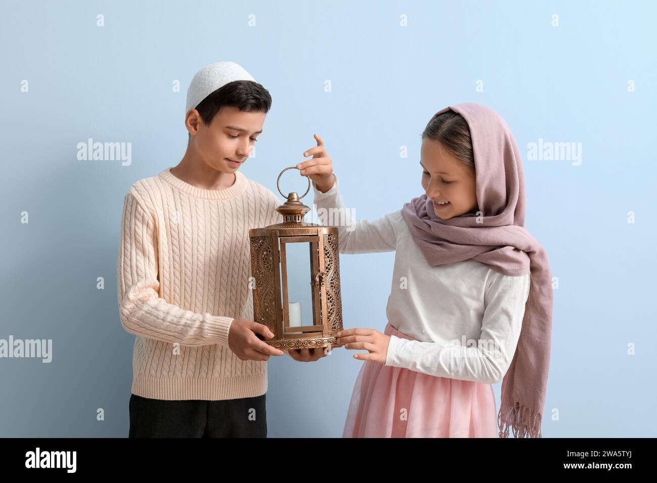 Little Muslim children with fanous lantern on light blue background ...