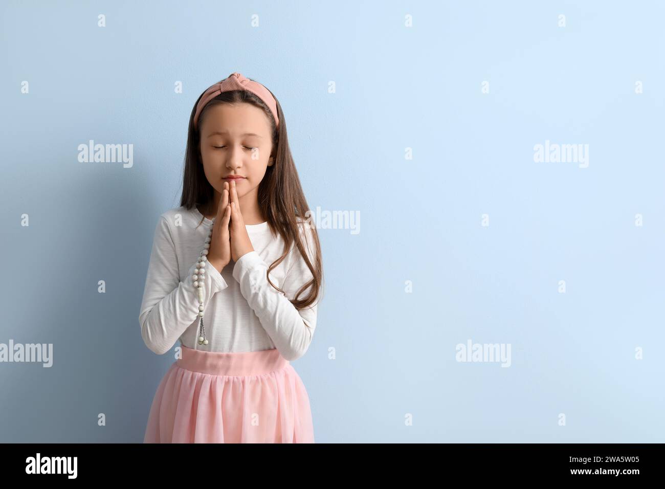 Praying little girl on light blue background Stock Photo - Alamy