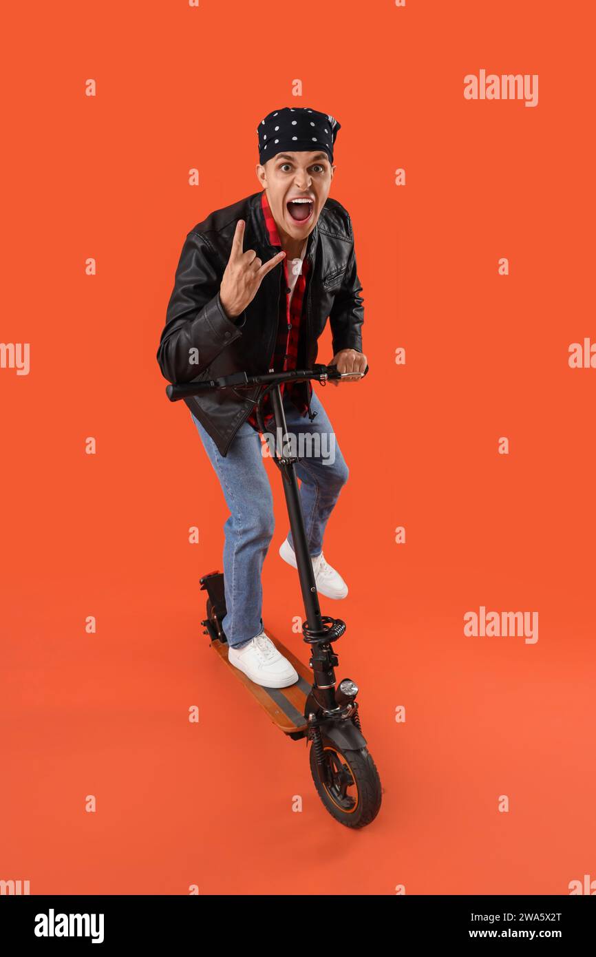 Cool young man with kick scooter showing "devil horns" on orange ...
