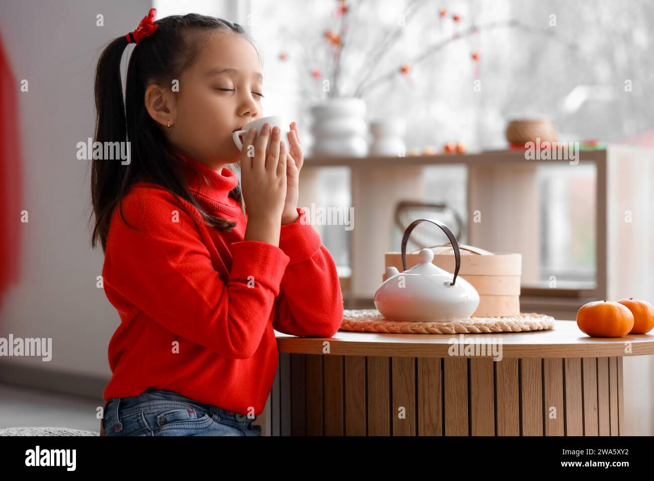 Cute little Asian girl drinking tea at home. Chinese New Year ...