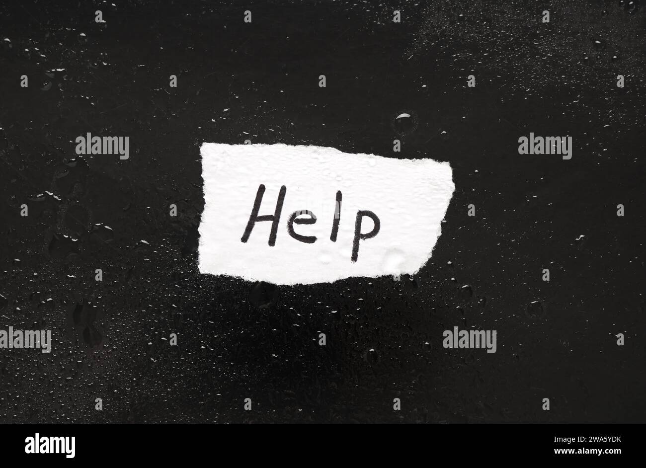 Paper piece with word HELP in water on dark background. Domestic ...