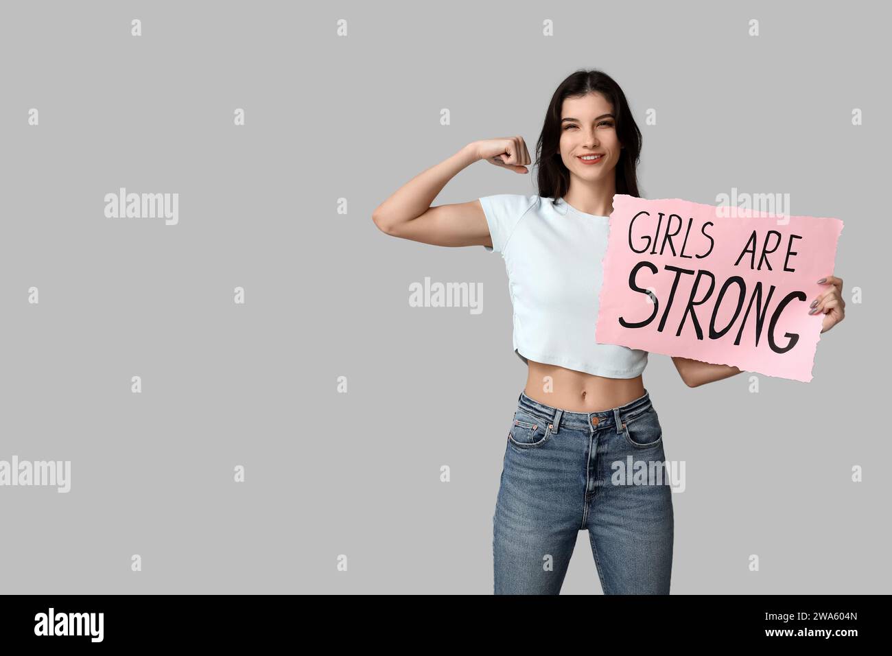 Young woman holding sign with text GIRLS ARE STRONG on grey background ...