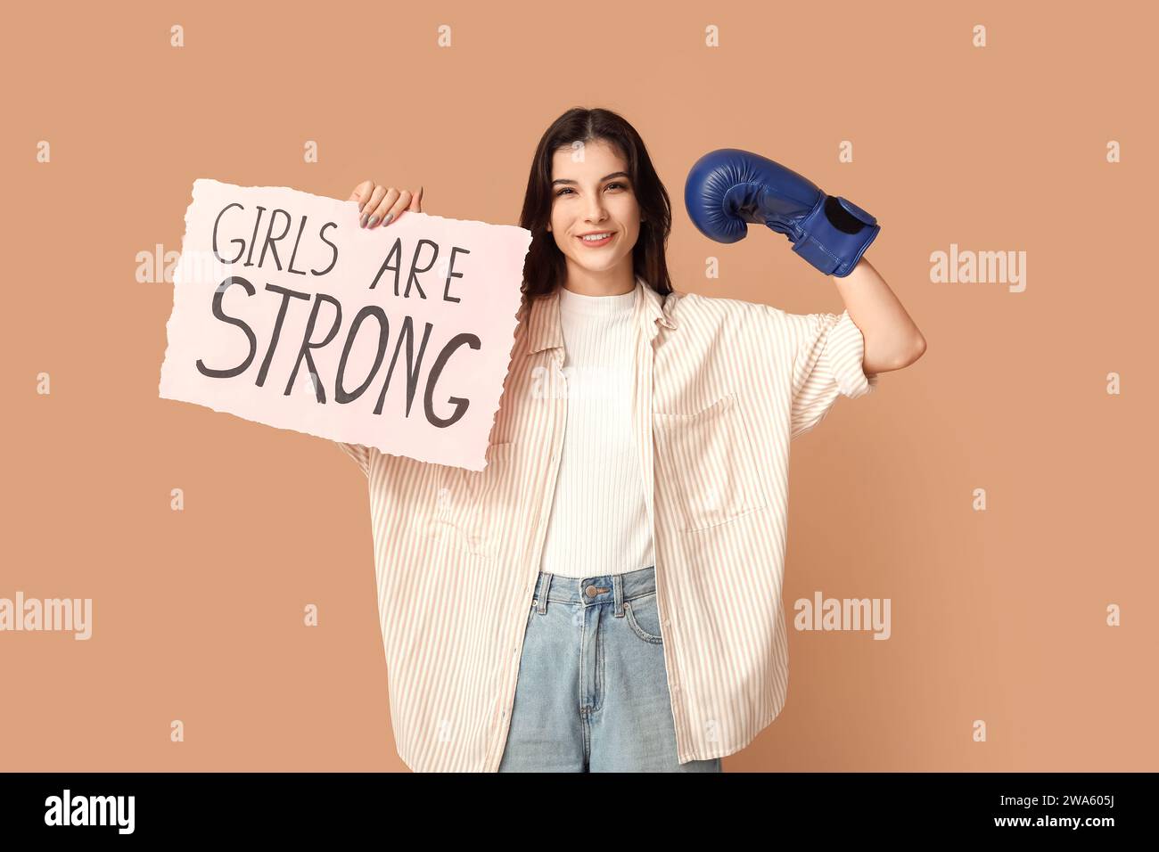 Young woman with sign GIRLS ARE STRONG and boxing glove on beige ...