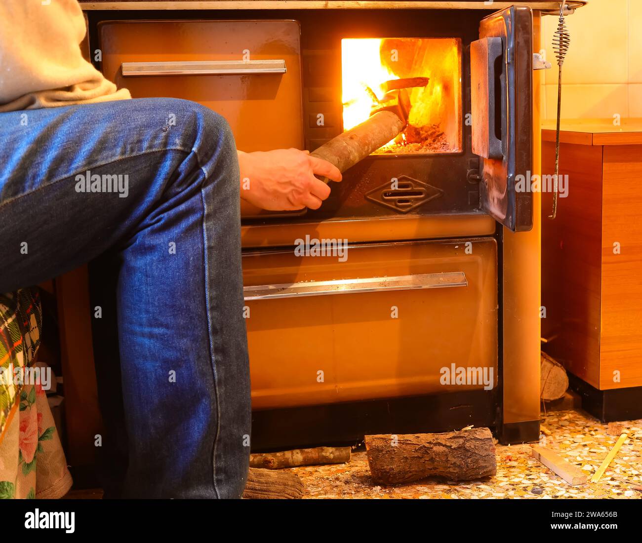 elderly person puts a piece of wood into the fire of the old wood ...