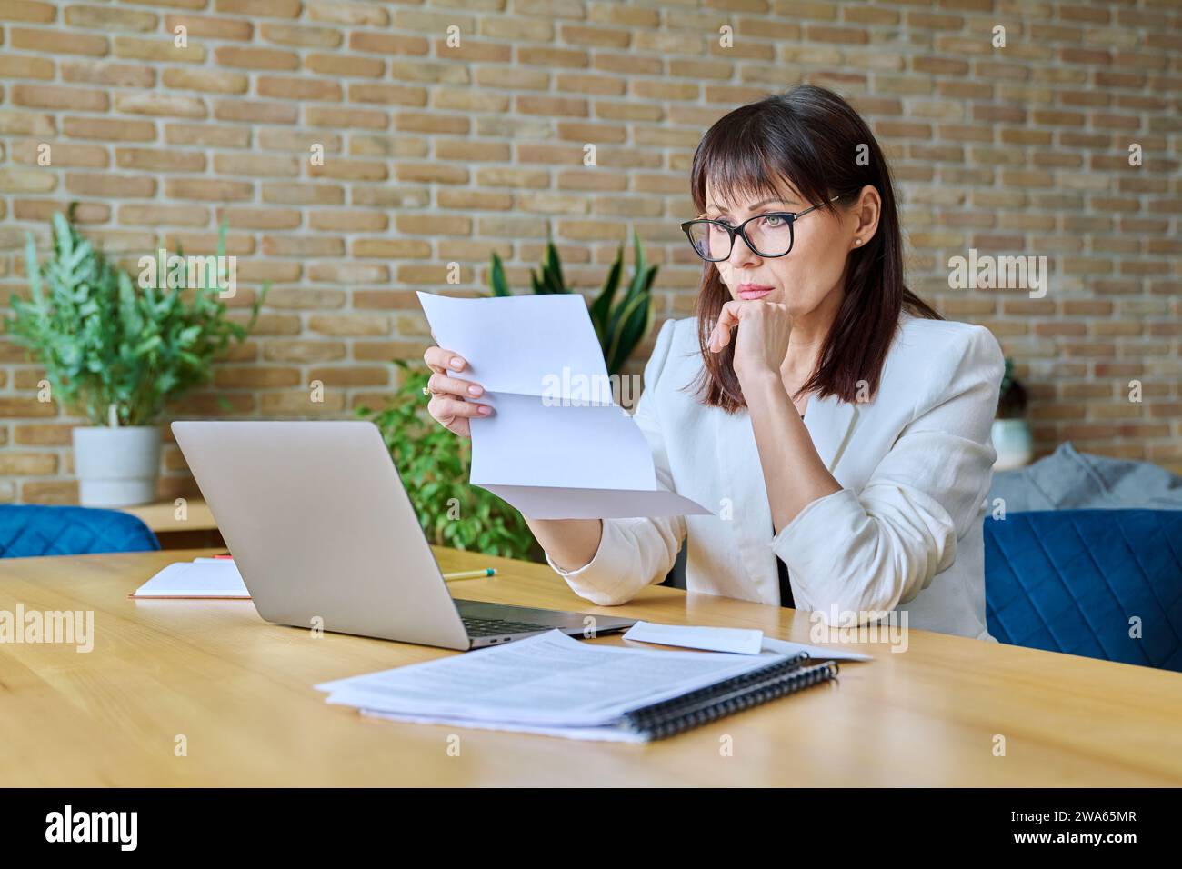 Serious mature businesswoman reading official letter, sitting in office ...