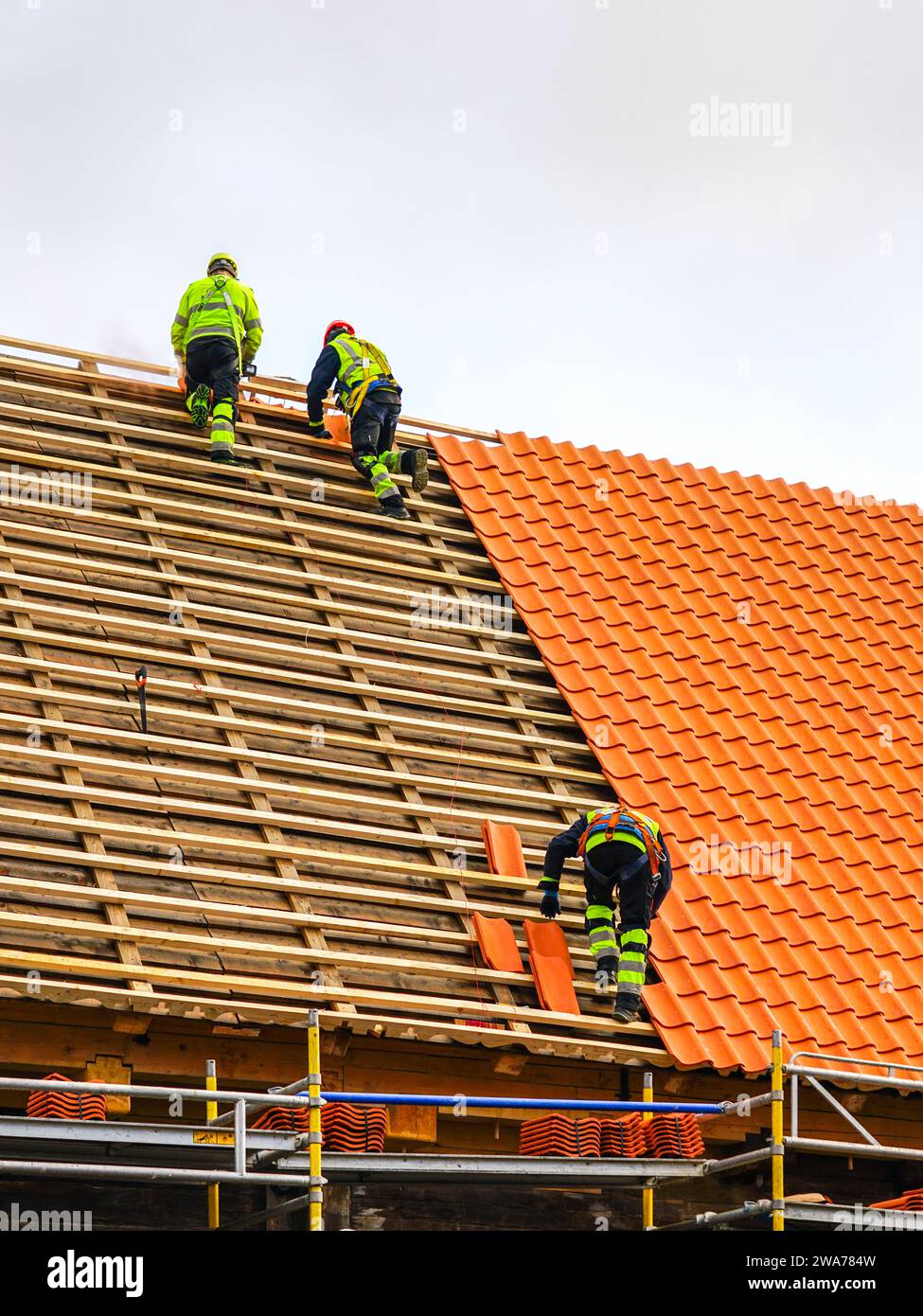 Three workers in protective workwear installing new clay tiles roof ...