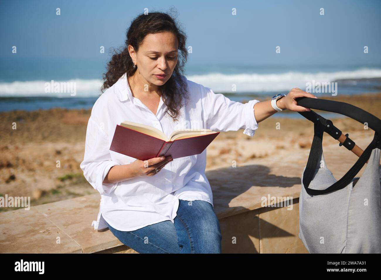 Happy young Latin American woman, mother pushing baby stroller, reading ...