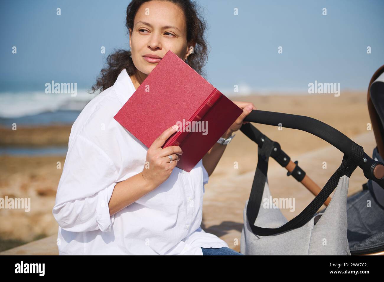 Beautiful woman holding a hard covered book near her face, dreamily ...