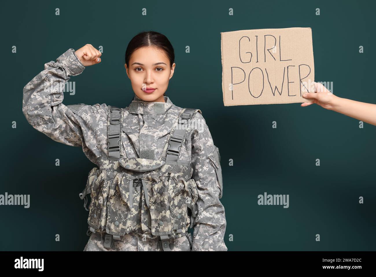 Young female soldier with sign GIRL POWER flexing muscles on green ...