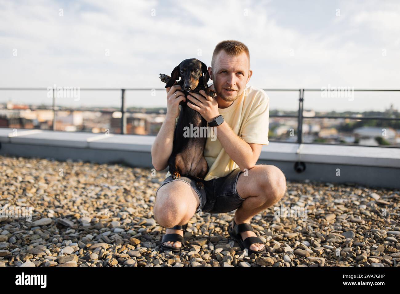 Happy caucasian man squatting and hugging dog on rooftop Stock Photo ...