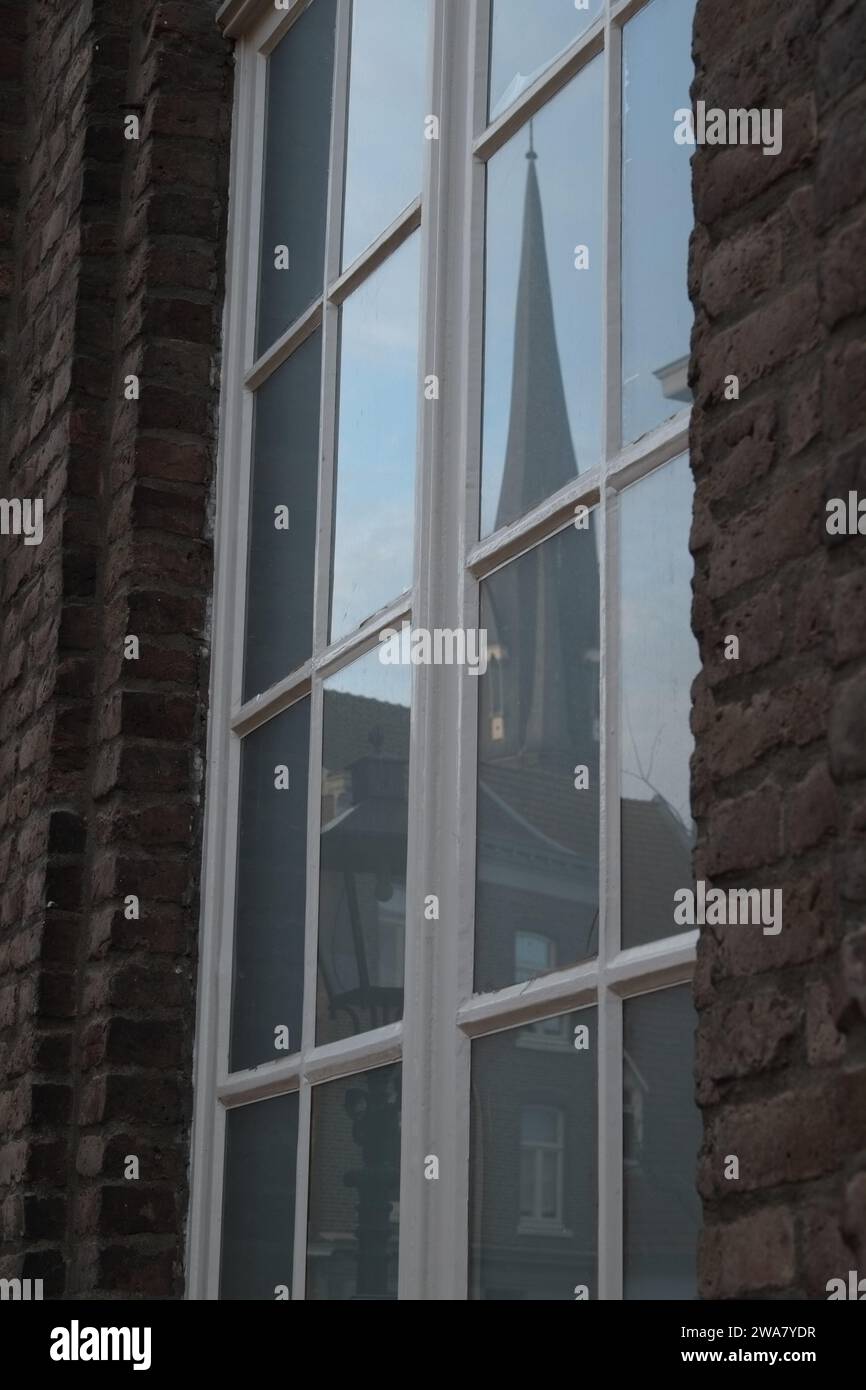 Reflection of an old church in a old wooden white framed tall window ...