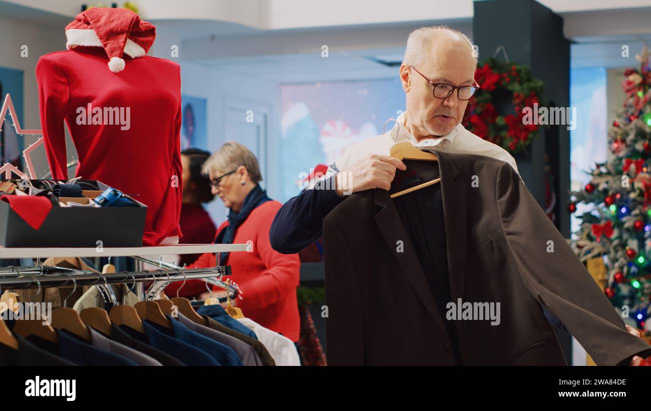 Senior man browsing blazers in festive clothing store during winter ...