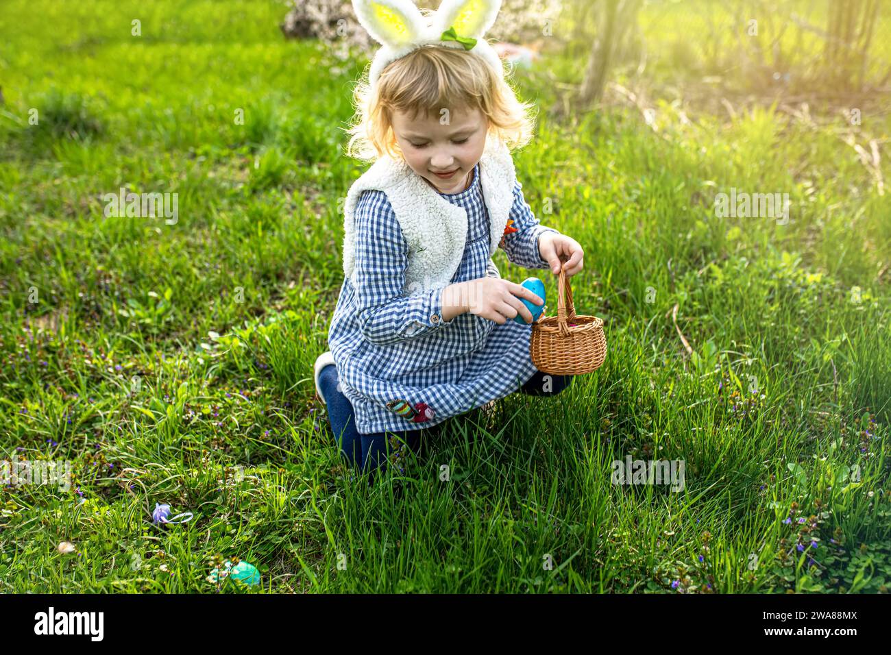 girl wearing bunny ears playing egg hunt on Easter. A child celebrates ...
