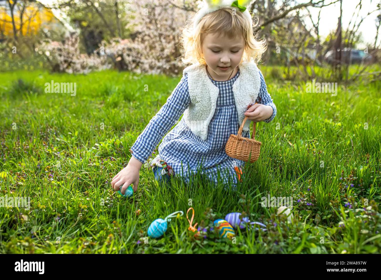 easter eggs hunt. Little girl with baskets in hands gathering colorful ...