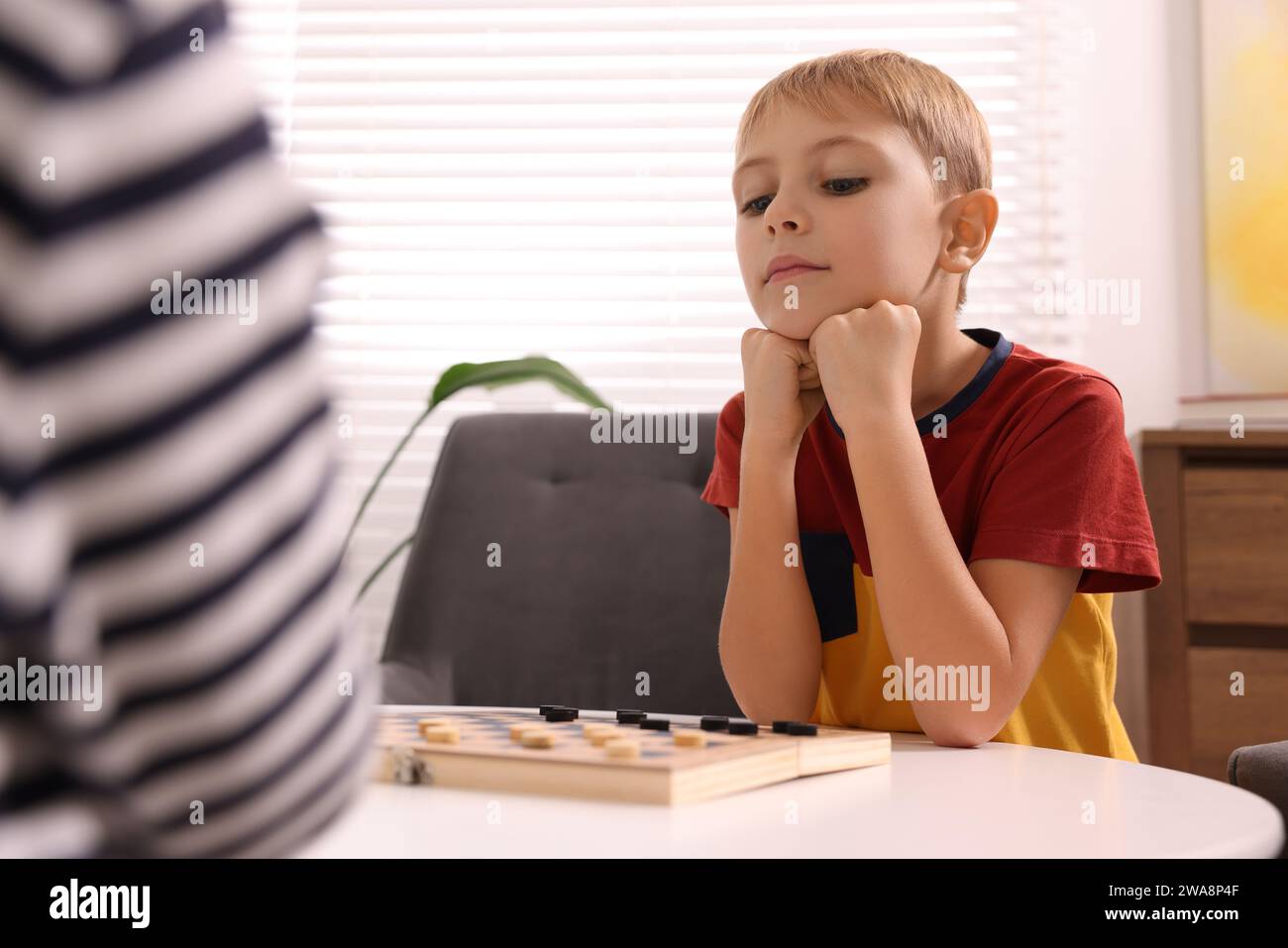 Cute boy playing checkers at coffee table indoors Stock Photo - Alamy