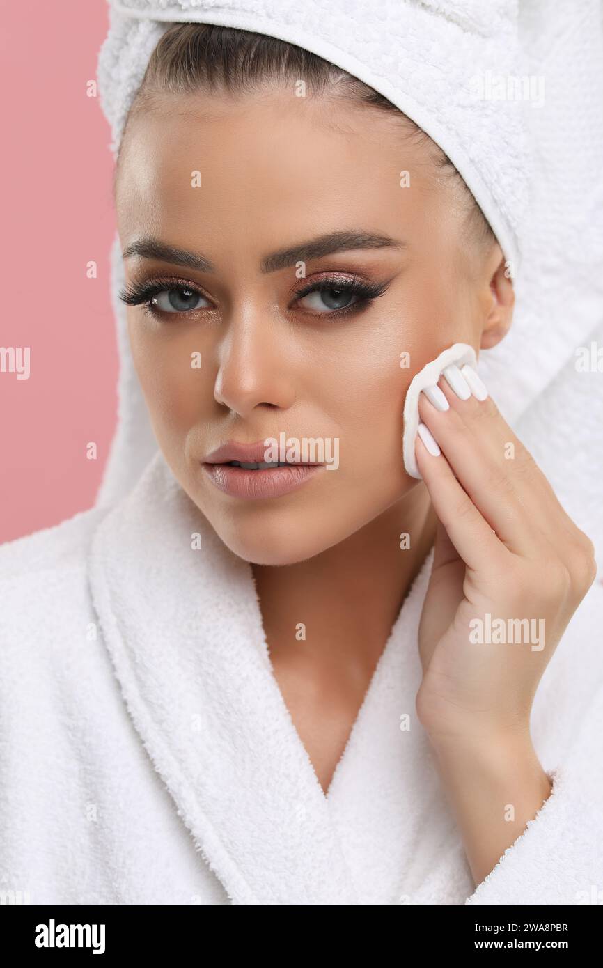 Beautiful woman removing makeup with cotton pad on pink background ...