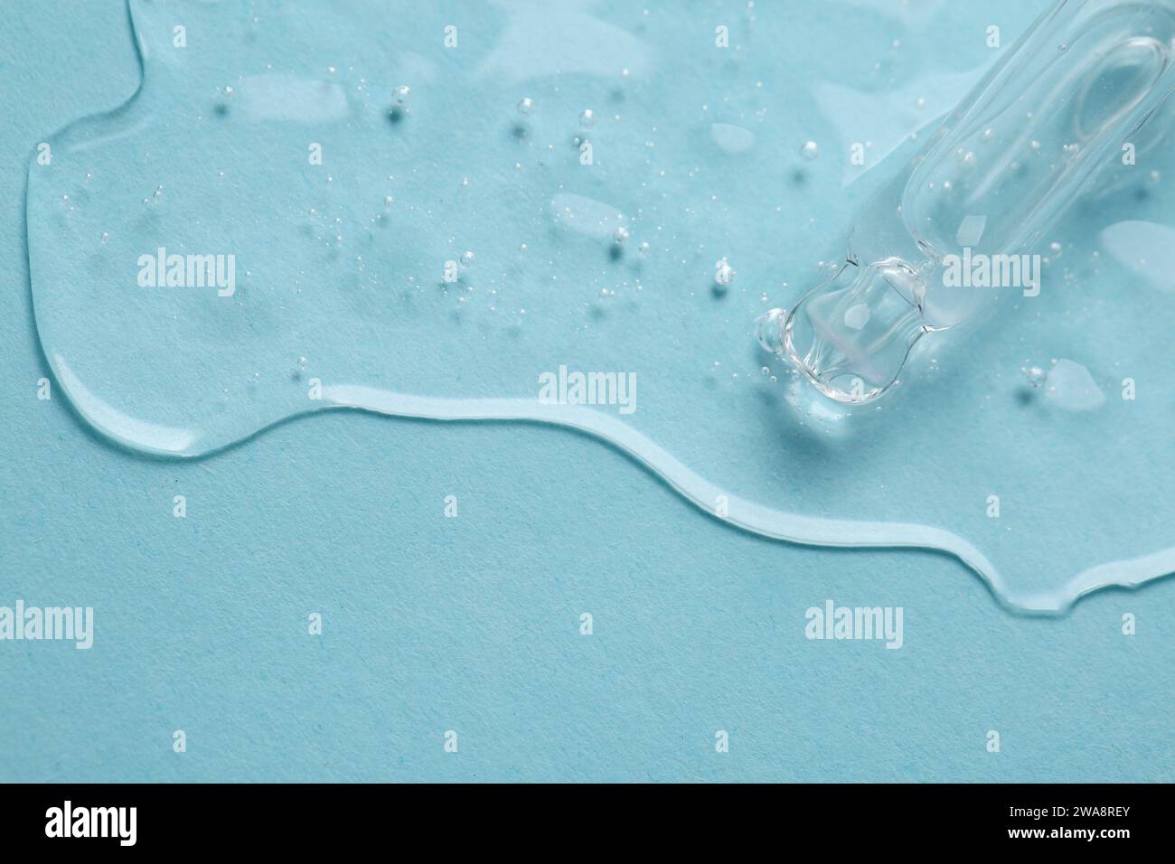 Dripping cosmetic serum from pipette onto light blue background, top ...