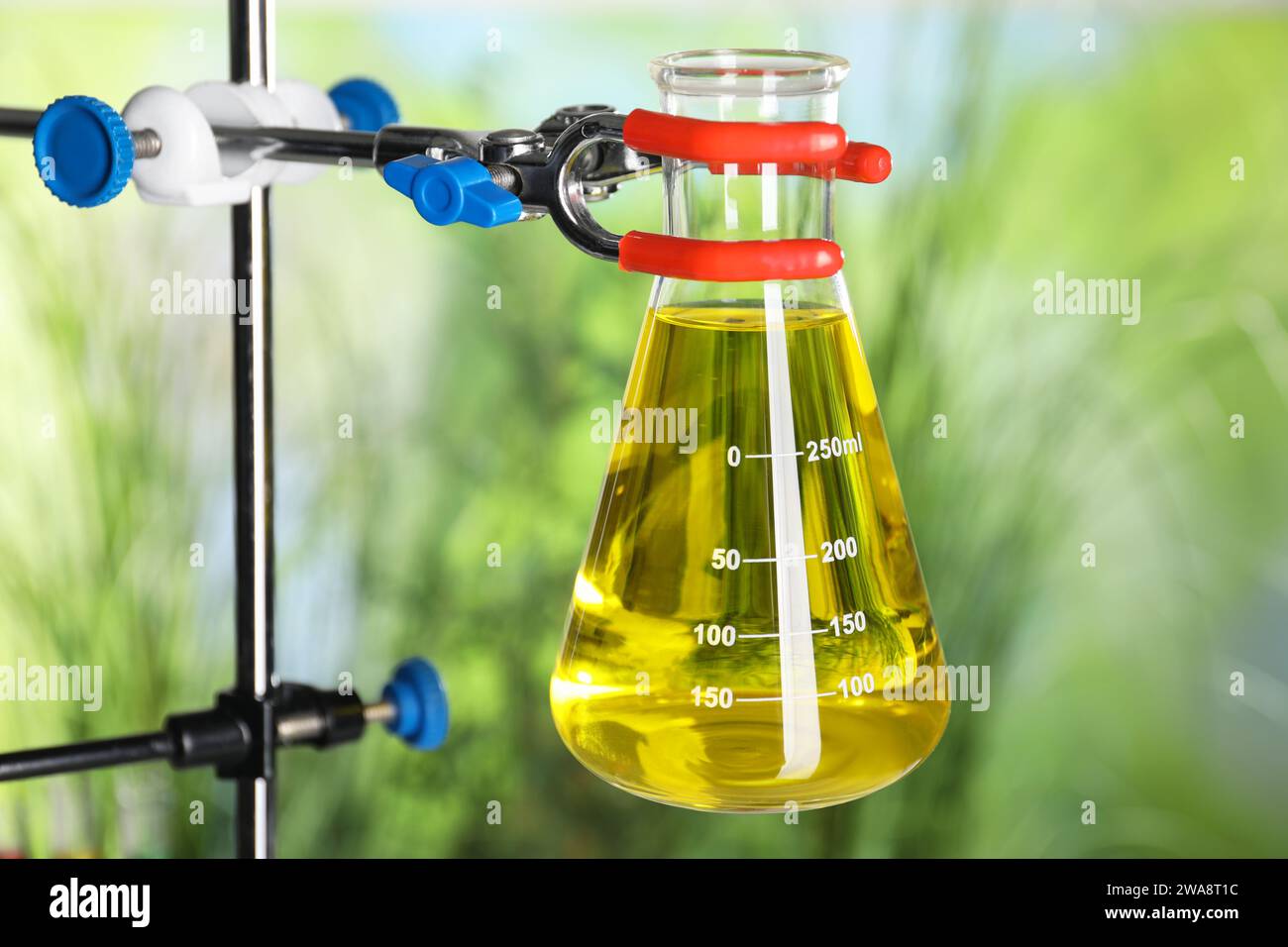 Retort stand and laboratory flask with liquid on blurred background ...