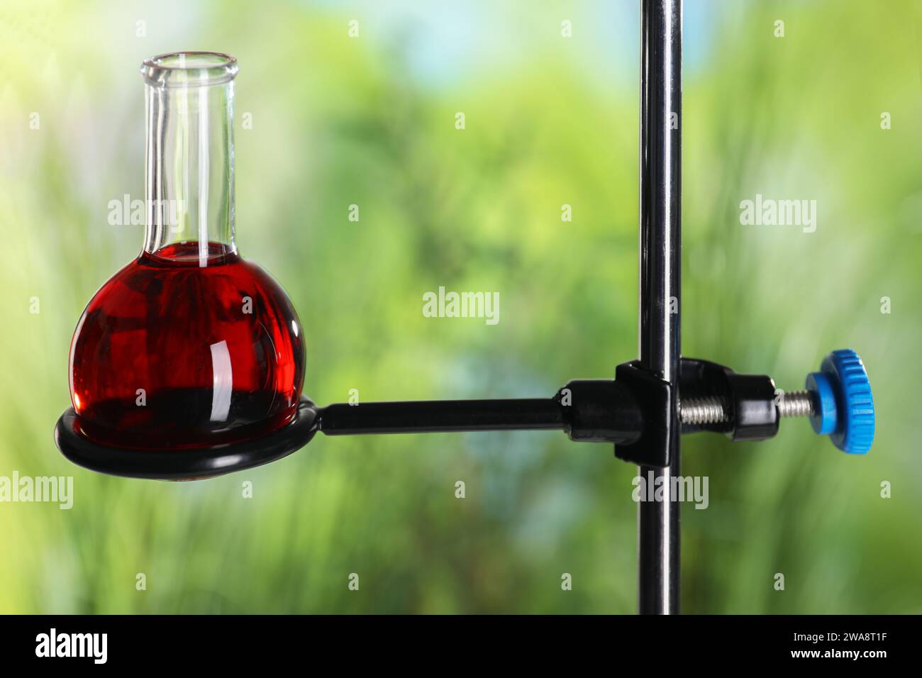 Retort stand and laboratory flask with liquid on blurred background ...