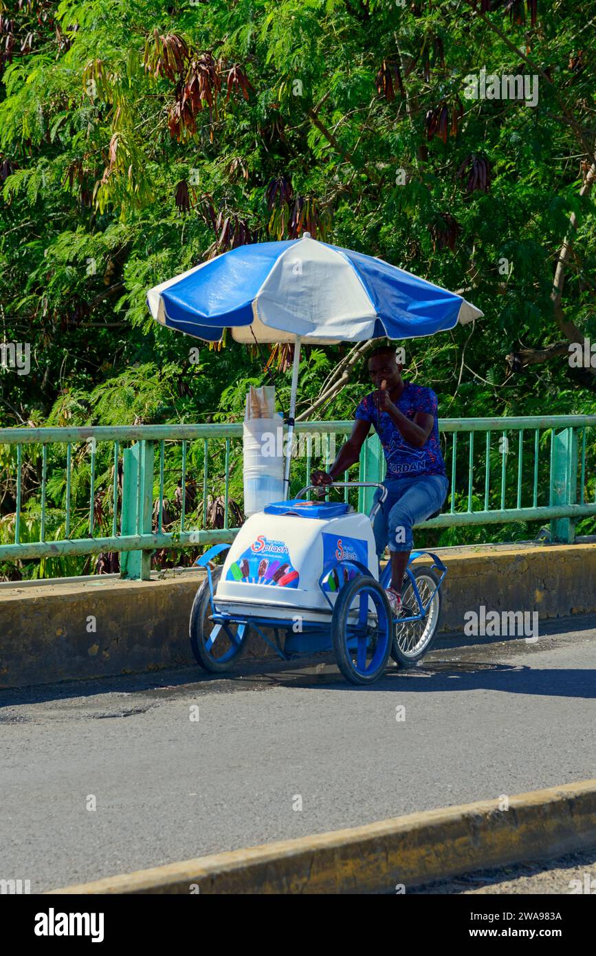 A street vendor selling ice cream rides his bicycle under a blue ...