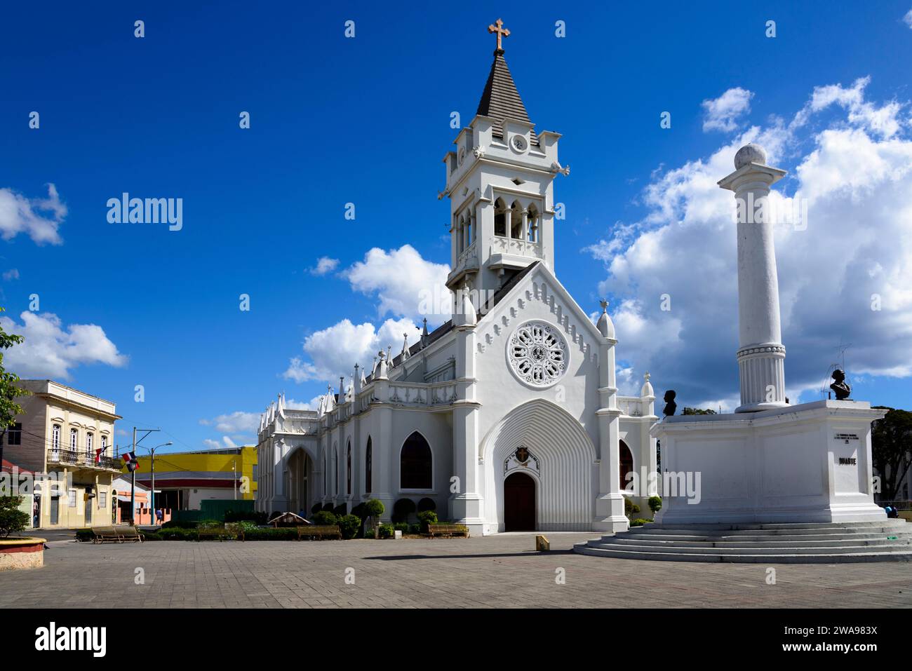 White church with pointed tower on a sunny square under a blue and ...