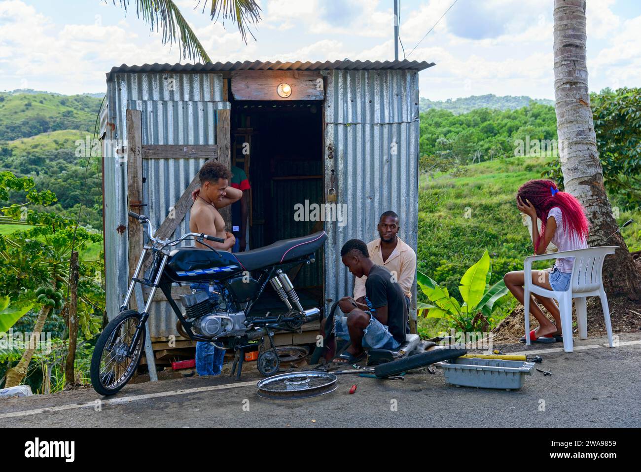 A group of people repairing a motorbike in front of a metal hut ...
