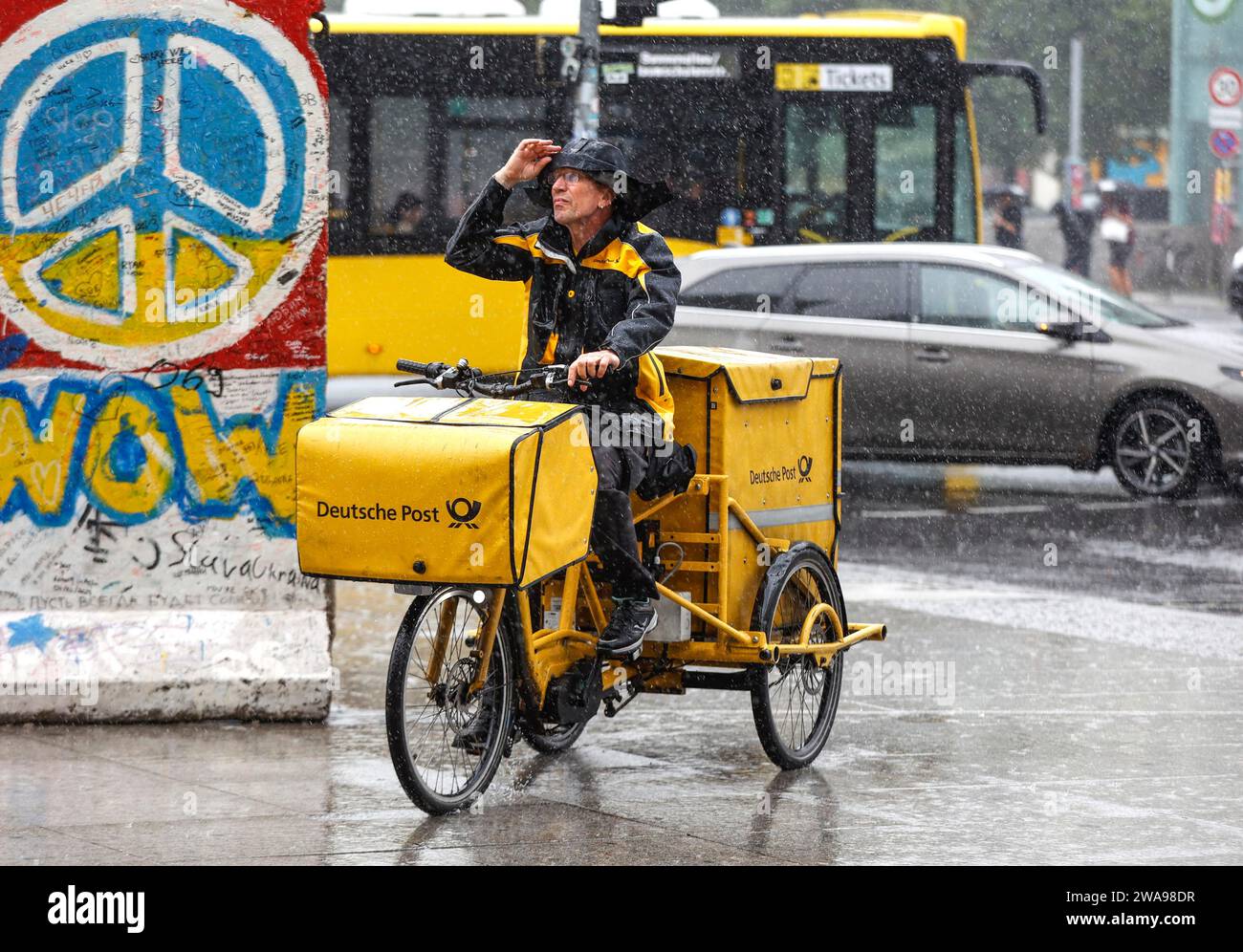 A DHL mail carrier rides his e-bike along a pavement in heavy rain ...