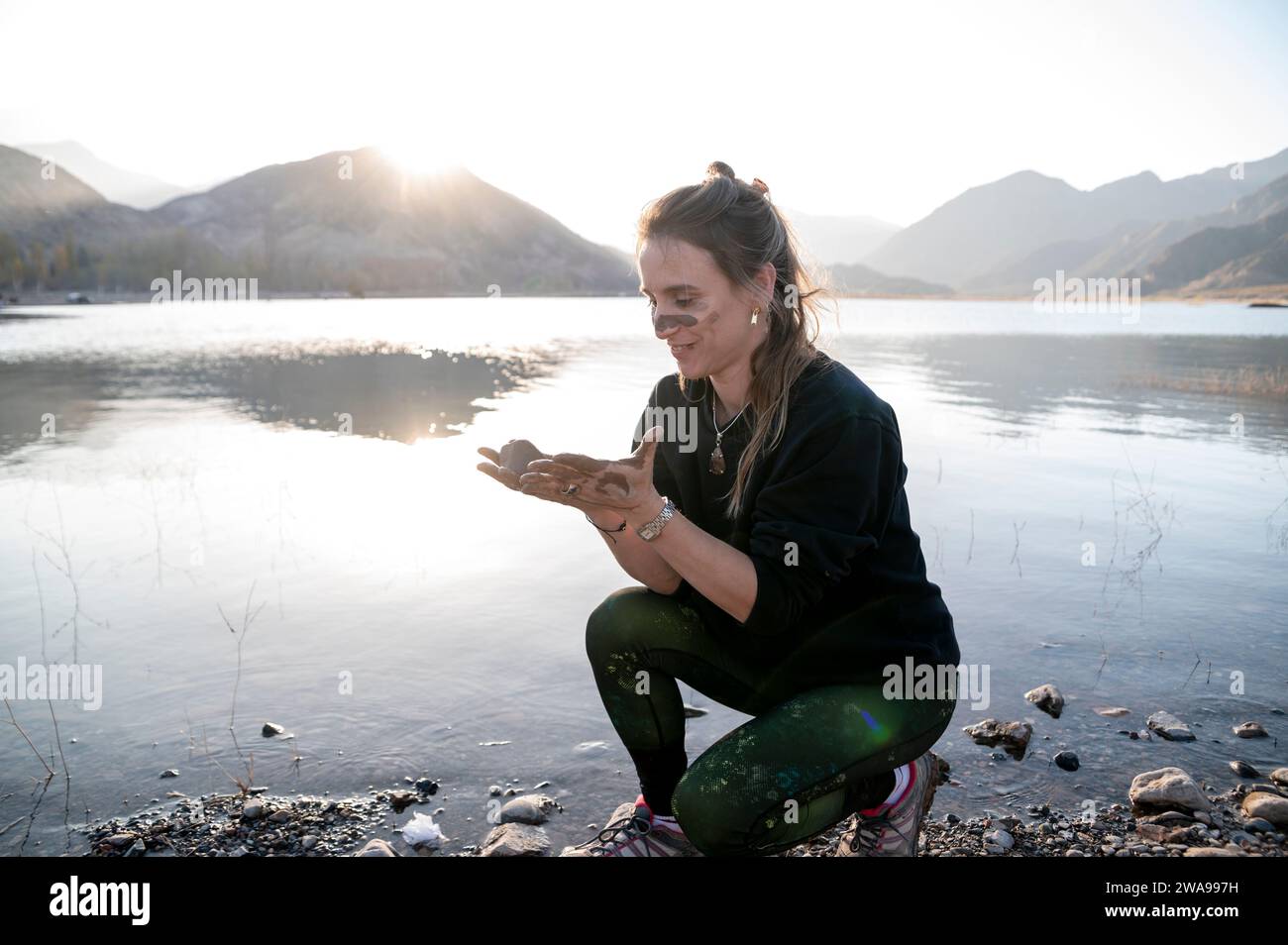 Woman putting mud on hands and face while enjoying outdoors in nature ...