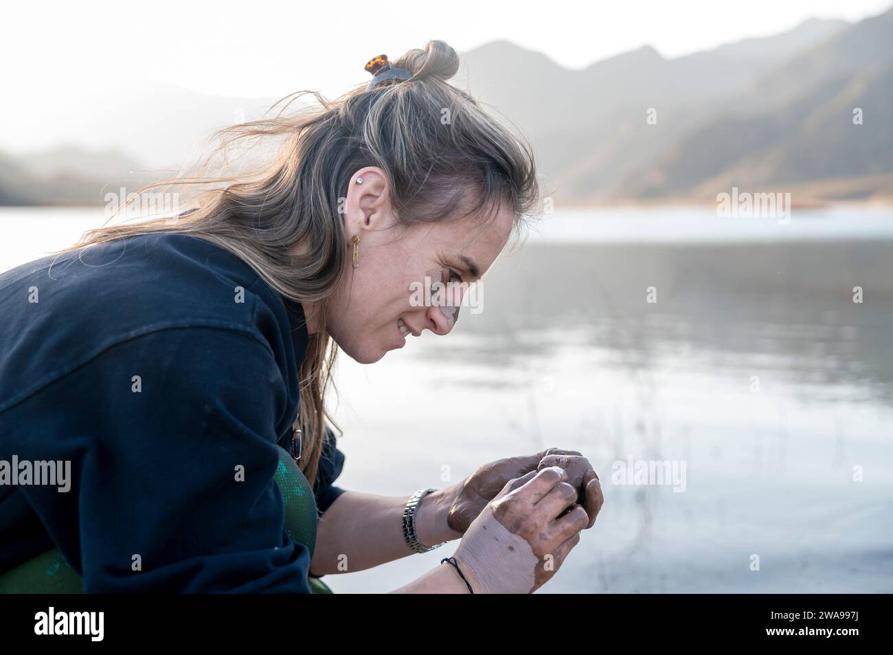 Woman putting mud on hands and face while enjoying outdoors in nature ...