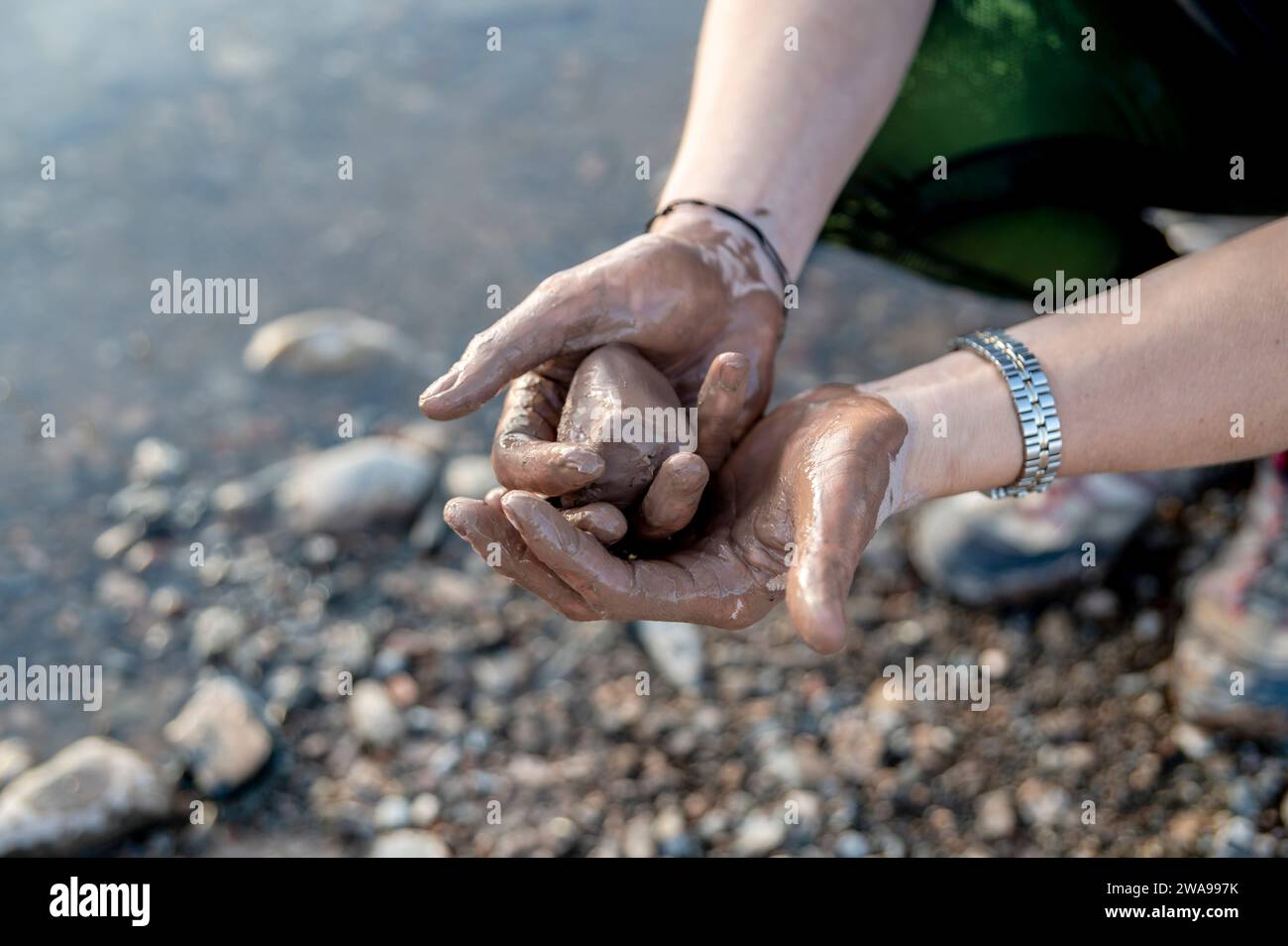 Woman putting mud on hands and face while enjoying outdoors in nature ...