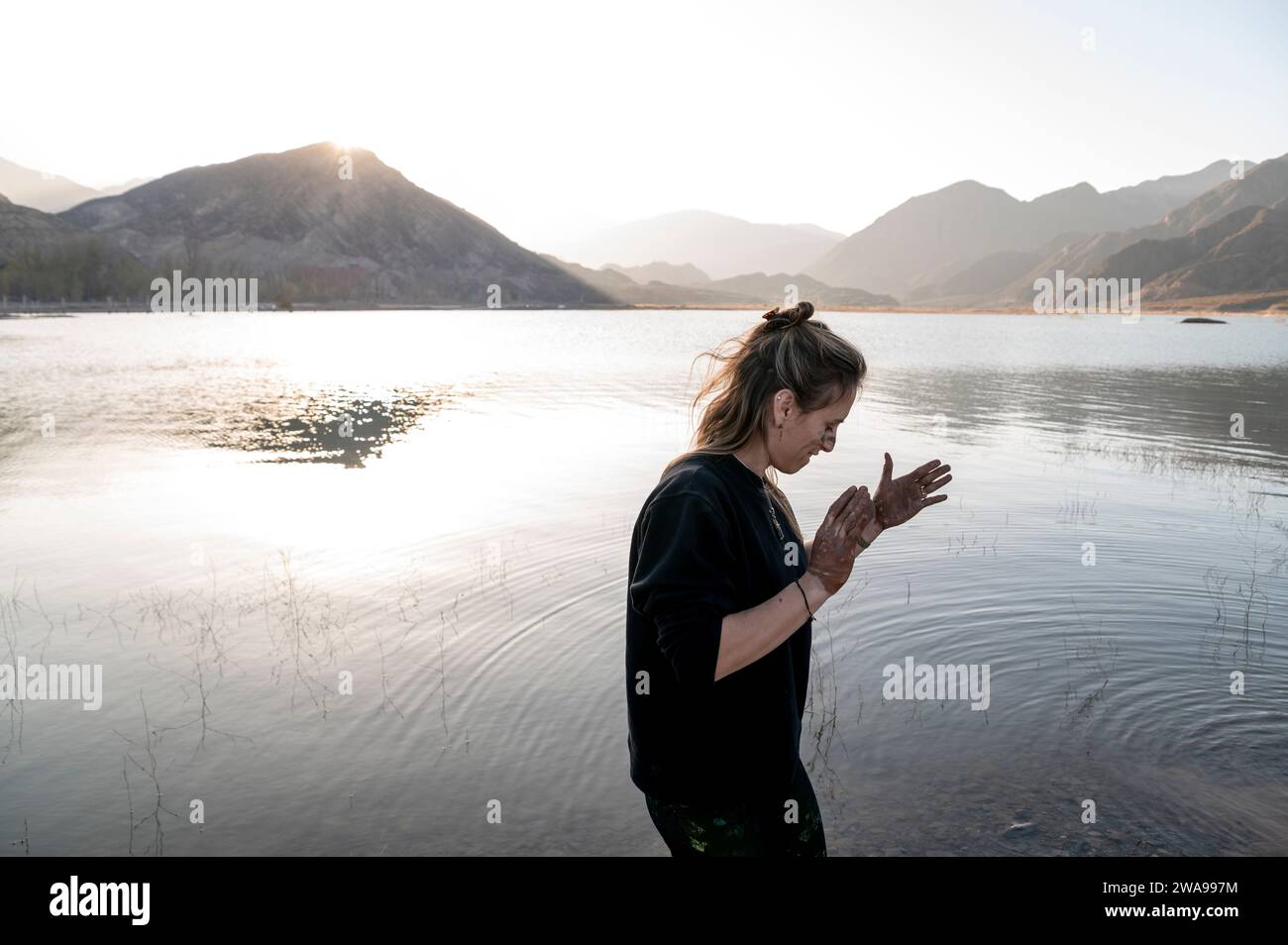 Woman putting mud on hands and face while enjoying outdoors in nature ...