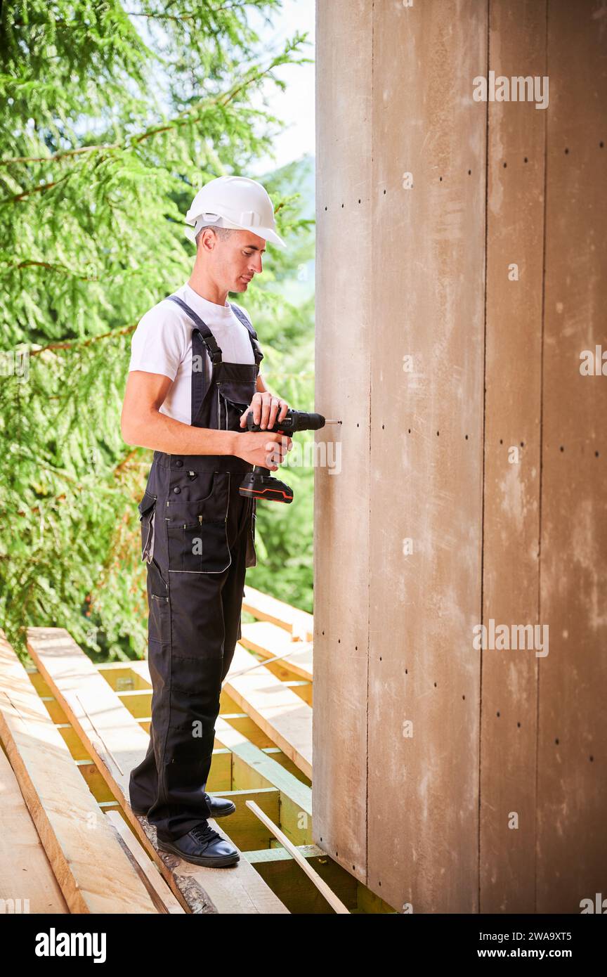 Carpenter constructing wooden framed house. Man worker cladding facade ...