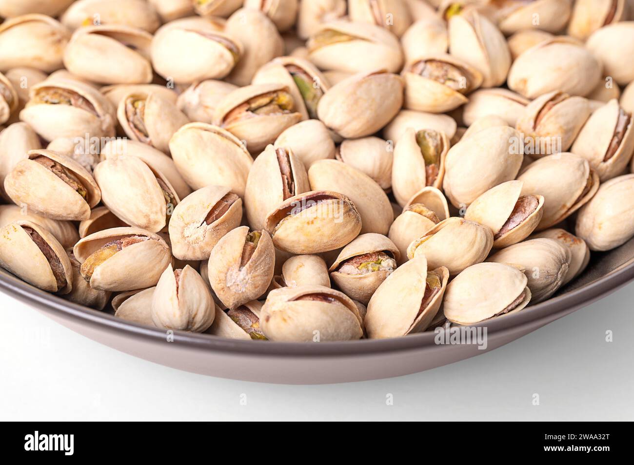Pistachios in their shells, roasted and salted, in a brown bowl. Crunchy roasted fruits of ...