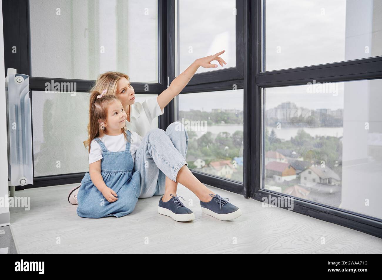 Woman and little girl sitting on the floor and looking and pointing out ...
