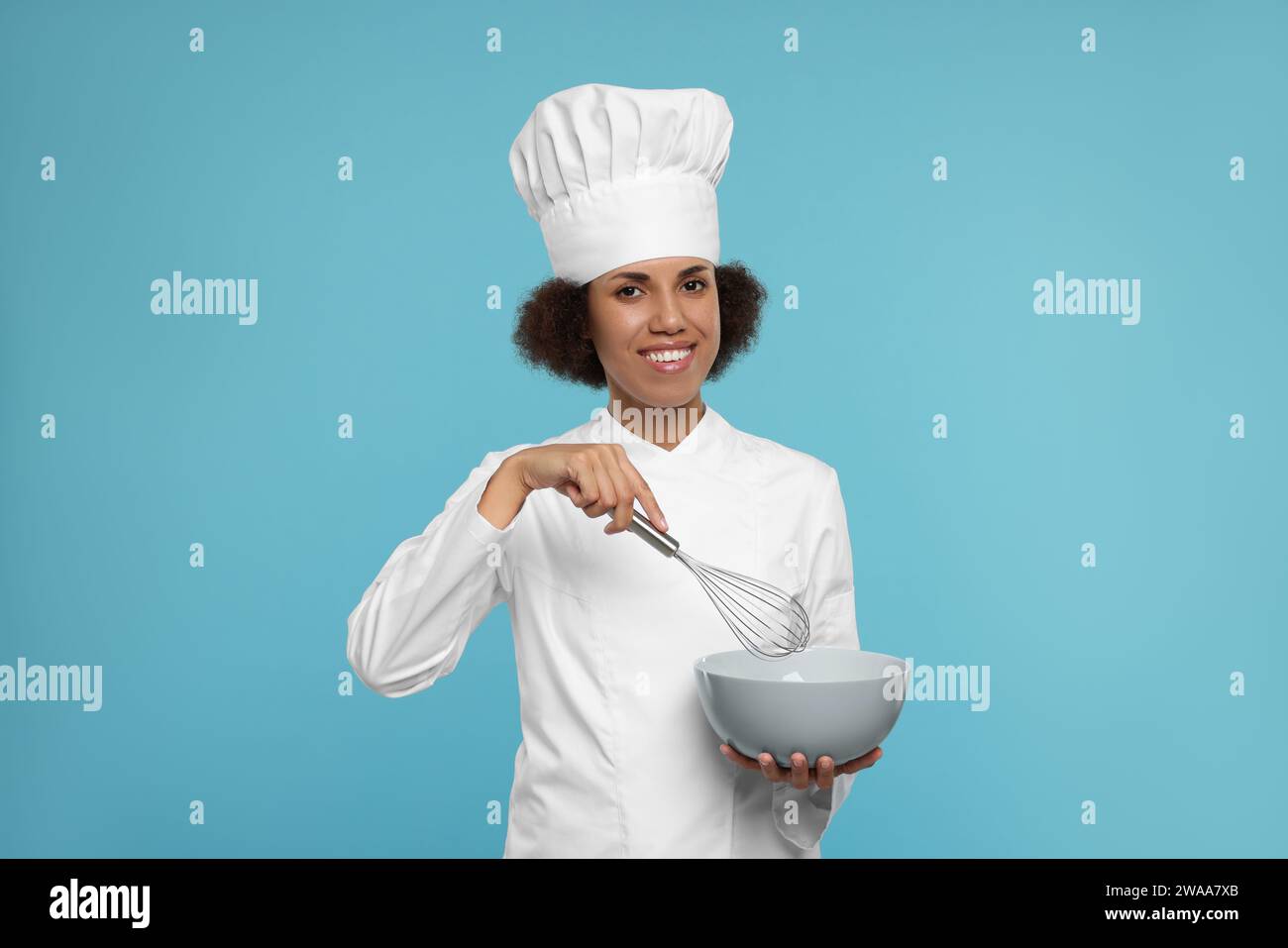 Happy female chef in uniform holding bowl and whisk on light blue ...