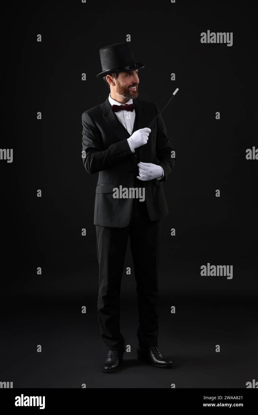 Happy magician holding wand on black background Stock Photo - Alamy