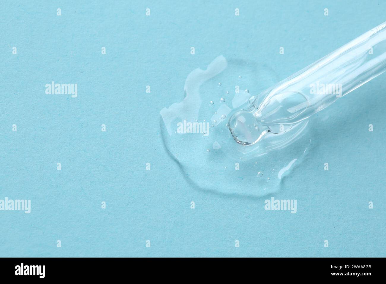 Dripping cosmetic serum from pipette onto light blue background, top ...