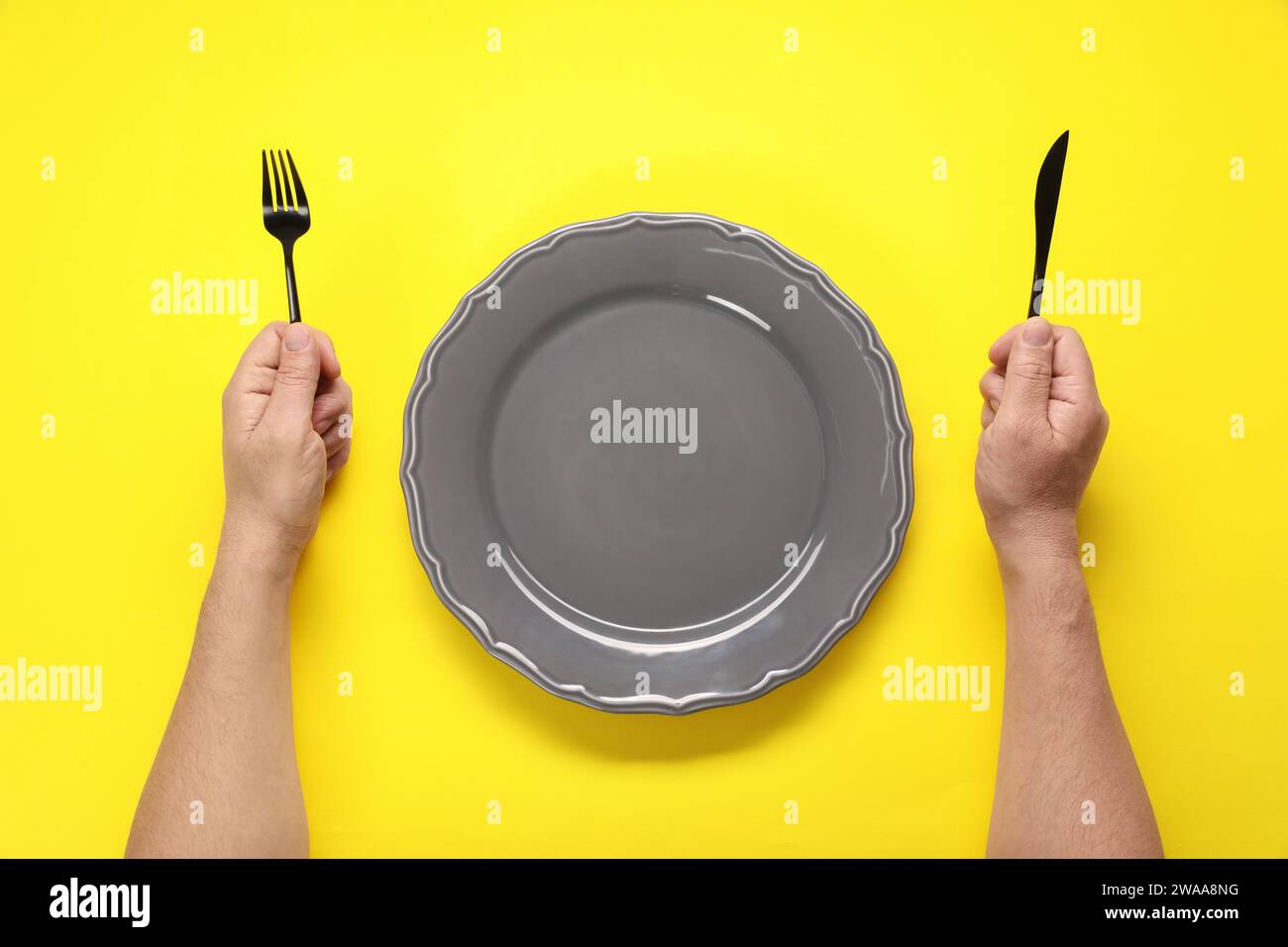 Man with fork, knife and empty plate at yellow table, top view Stock ...