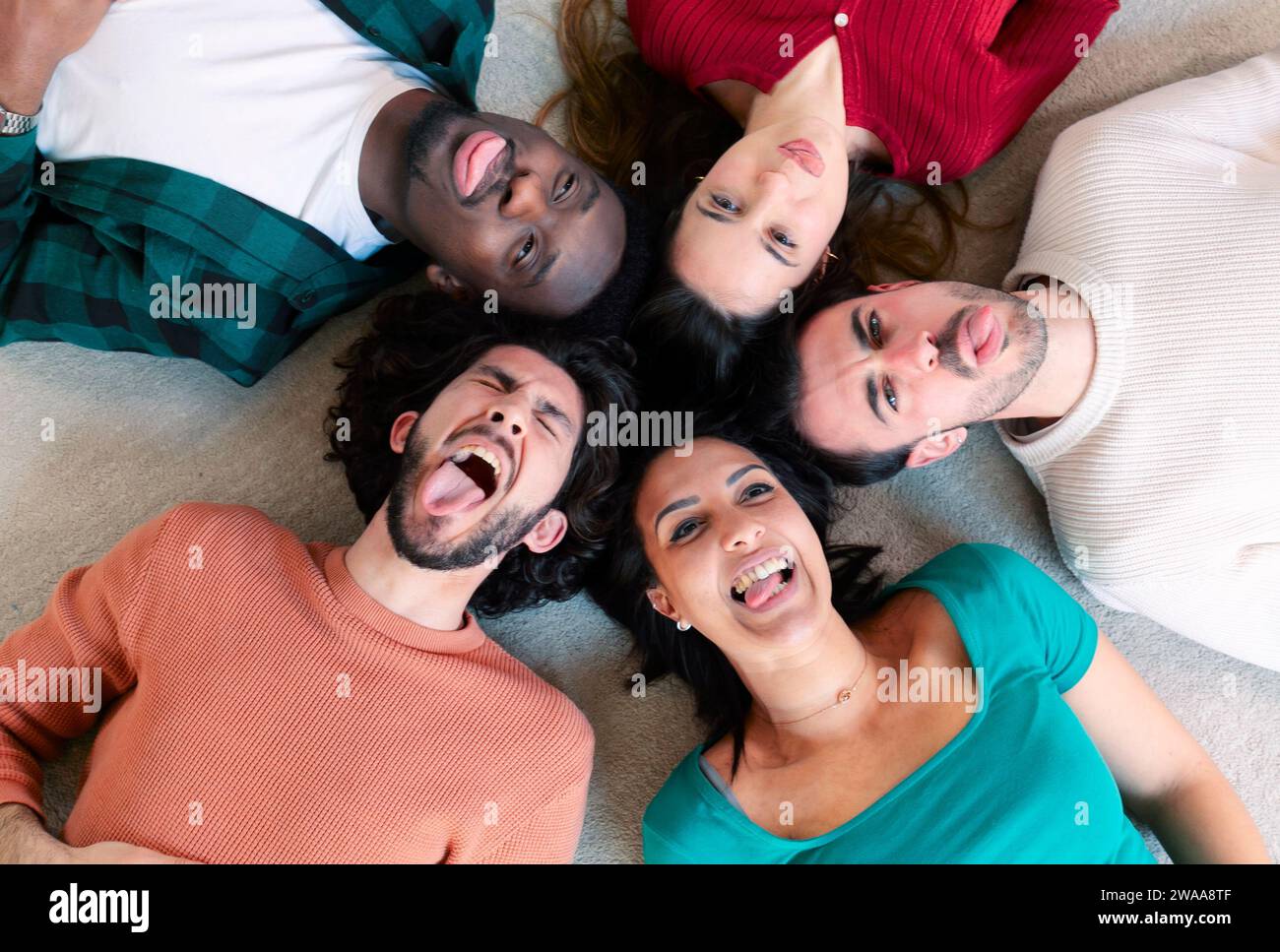 Diverse group of friends lying down taking silly selfies in circle ...